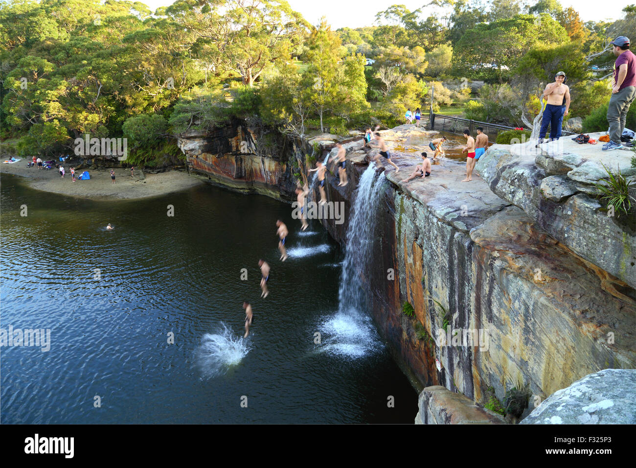 A crowd watches as a man jumps off the cliff into a swimming hole at ...