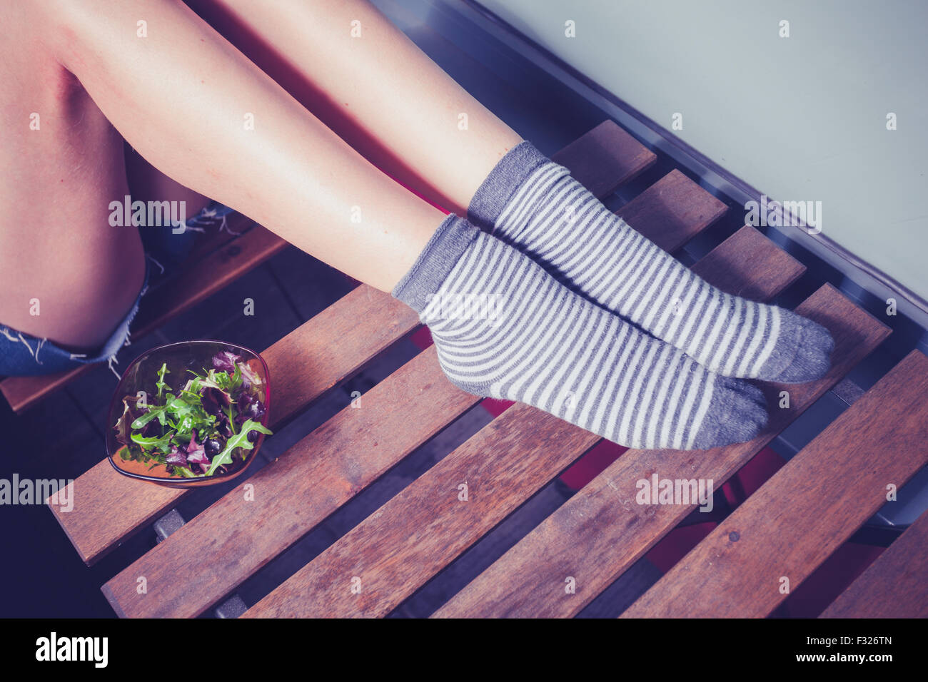 Young woman resting her legs on a table next to a bowl of salad Stock ...