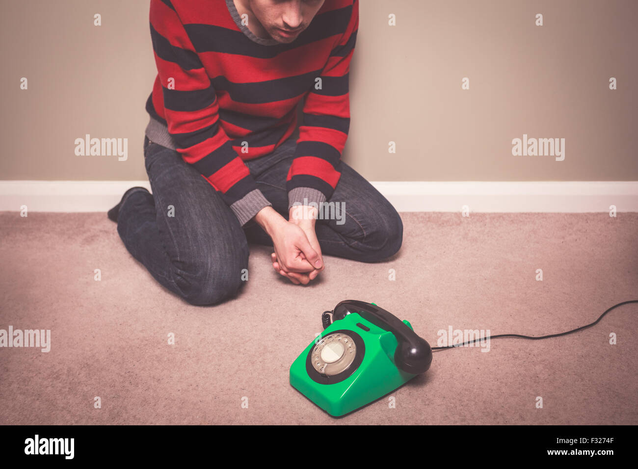 A young man is sitting on the floor and is desperately waiting for a ...