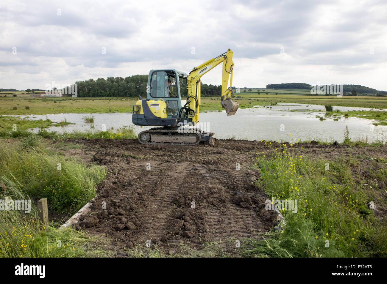 Small digger working on water dam and sluice gates at Deepdale Marsh ...