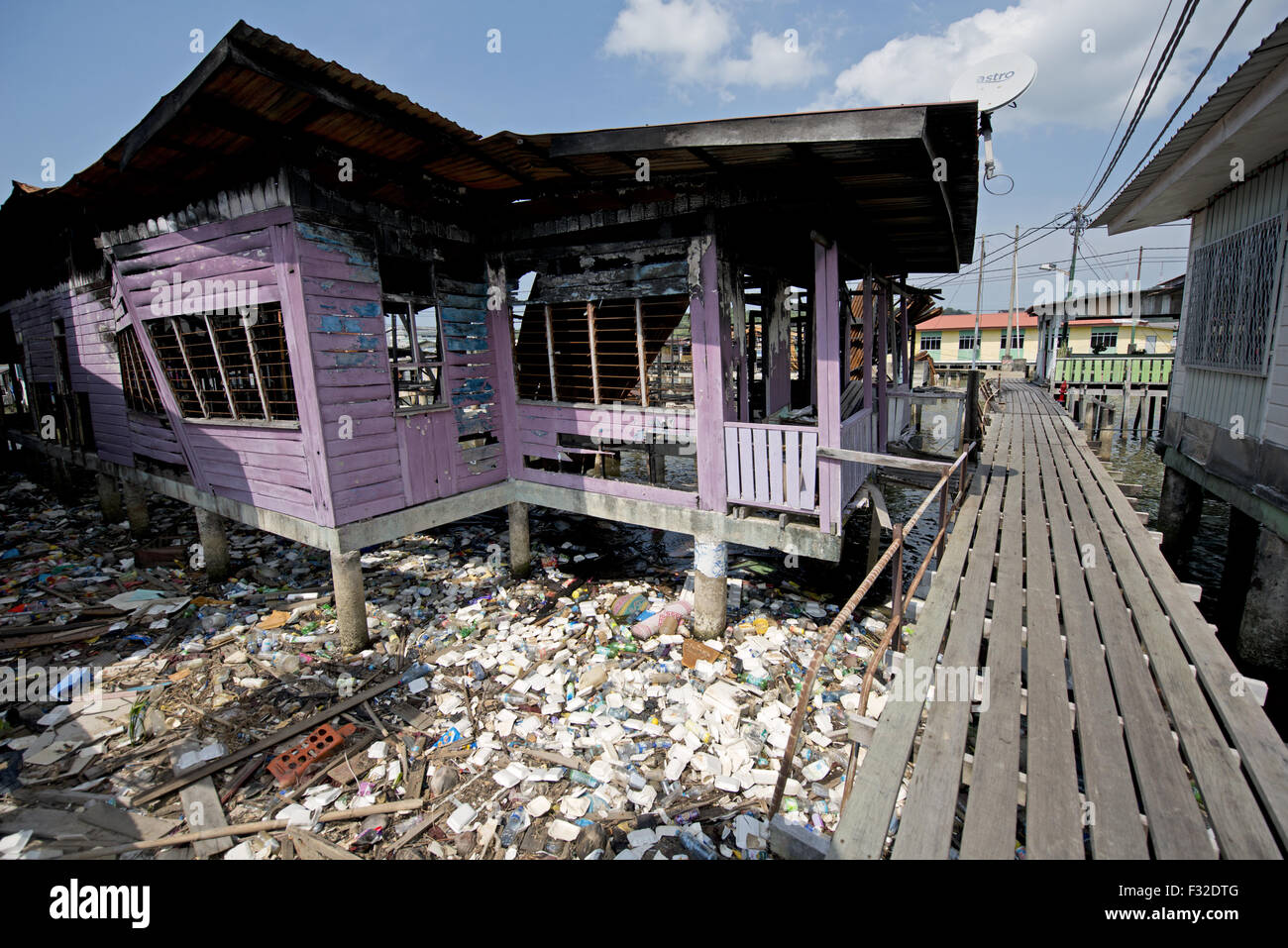 Walkway and burnt-out shack on stilts with washed up rubbish from river ...