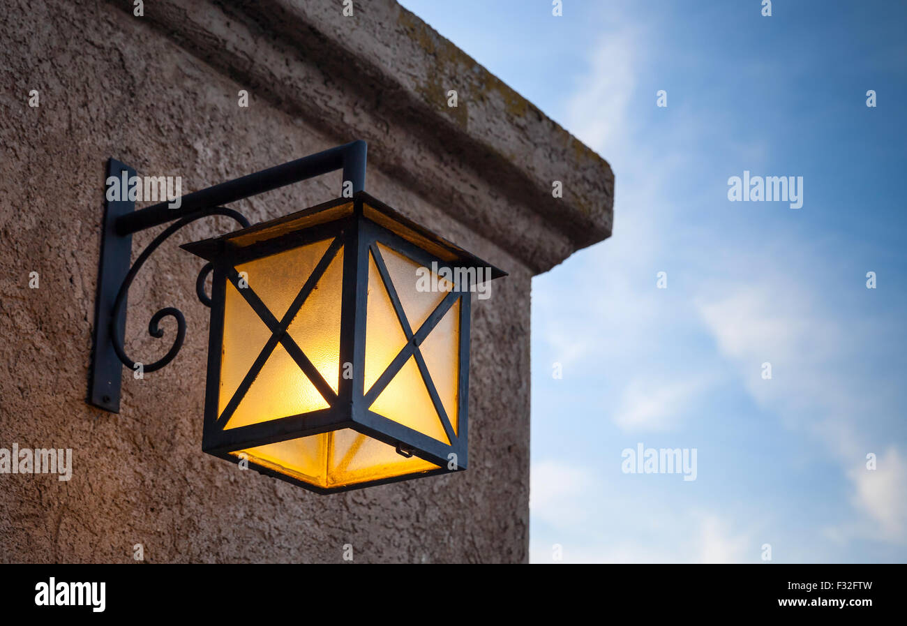 Ancient street lamp mounted on stone wall over blue sky background ...