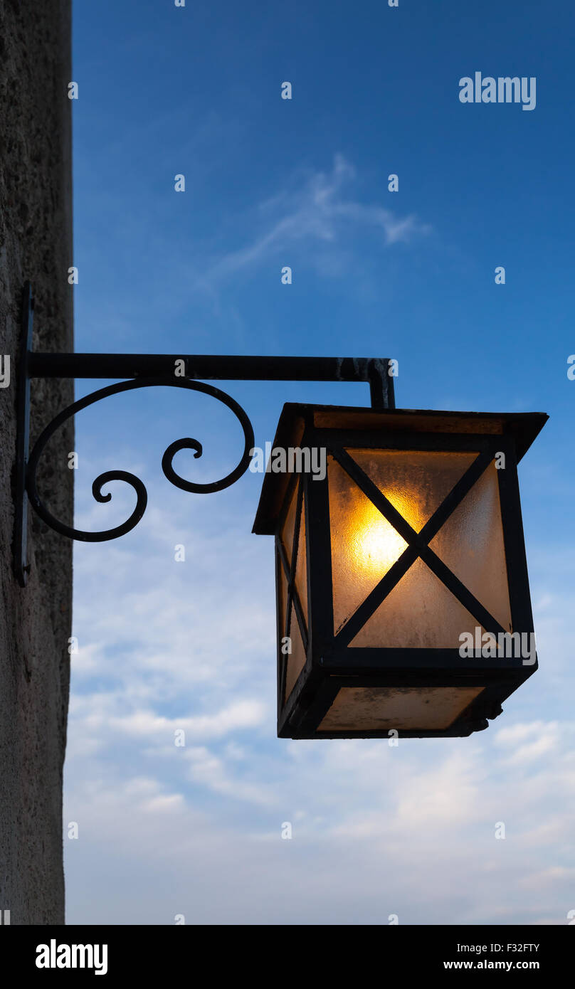 Ancient street lamp mounted on stone wall over dark blue sky background ...