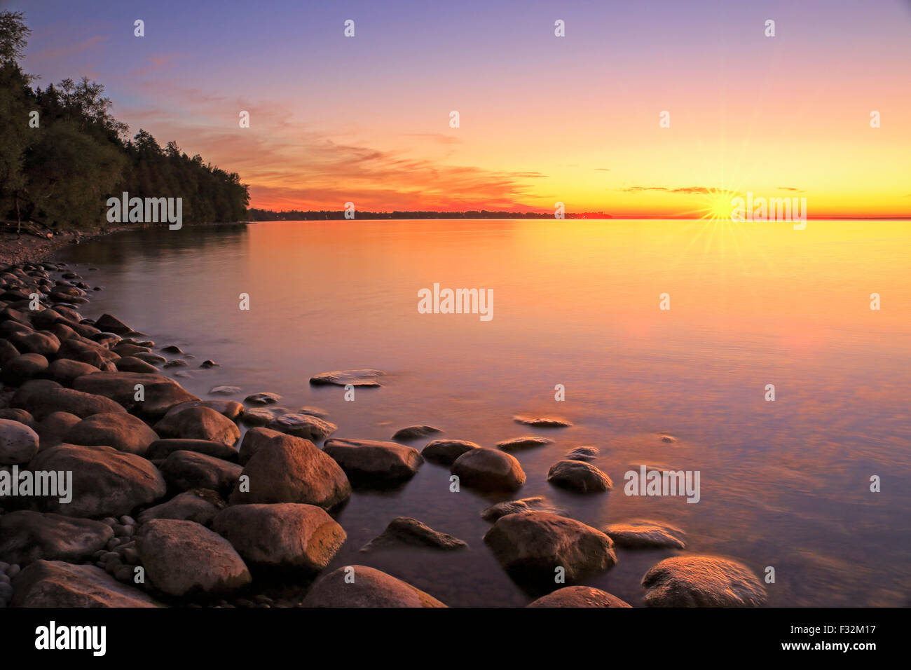 Tranquil smooth water and beach pebbles and rocks basking in beautiful ...