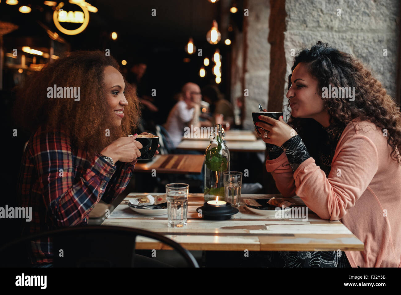 Side view portrait of two young women talking and drinking coffee in a ...