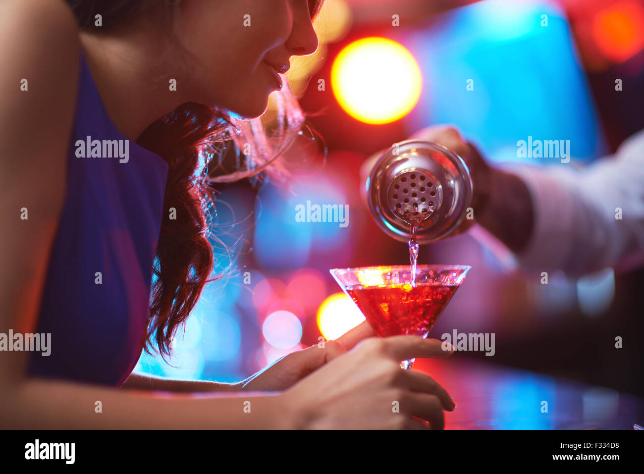 Girl looking at drink in martini glass while barman pouring cocktail ...