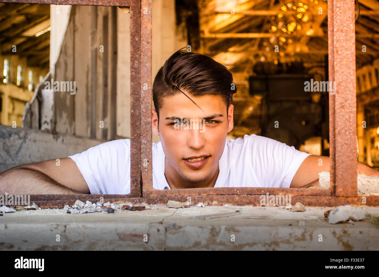 Attractive young man at rusty window with happy expression on his face ...