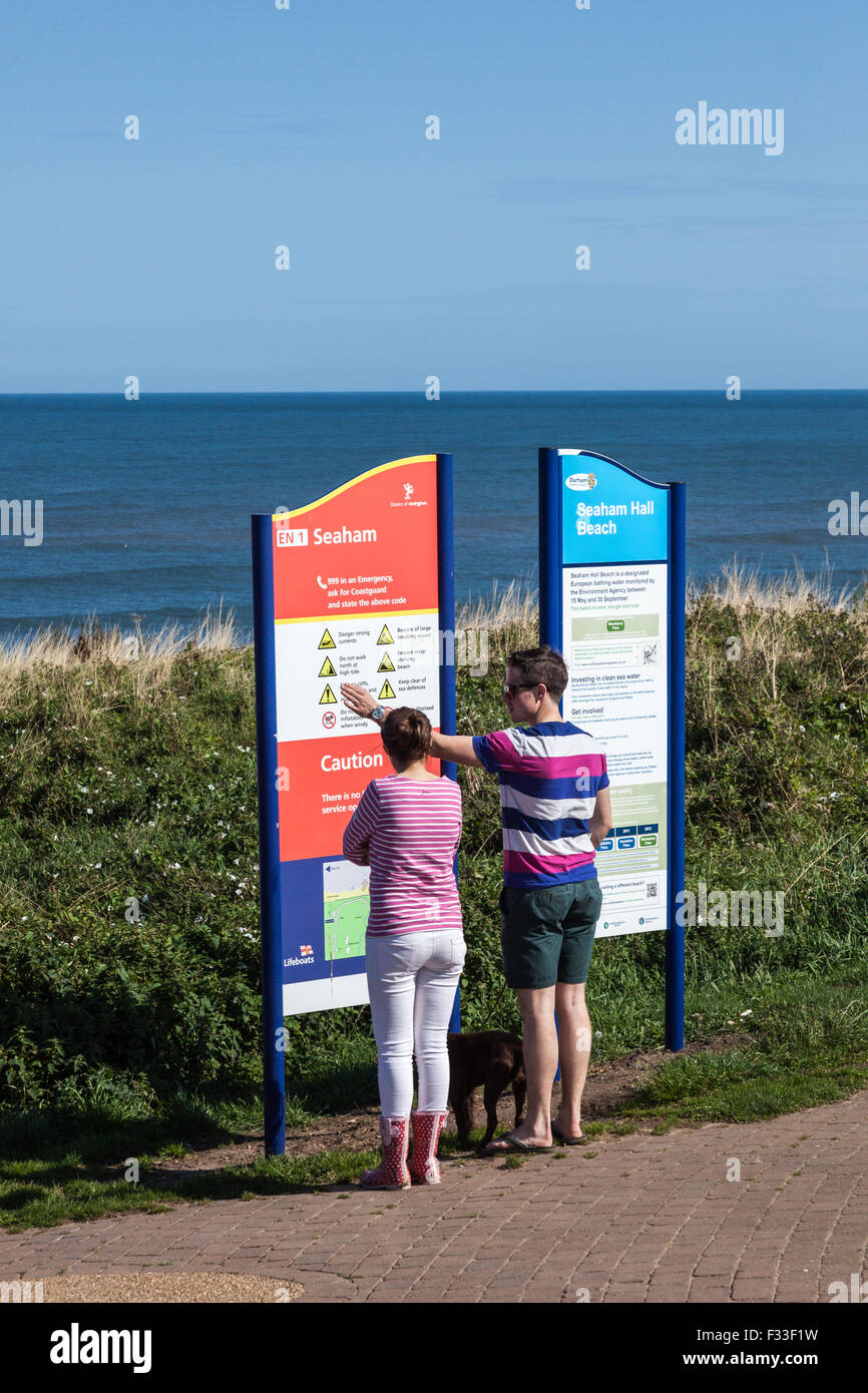 A man and woman couple with a dog look at beach information signs ...
