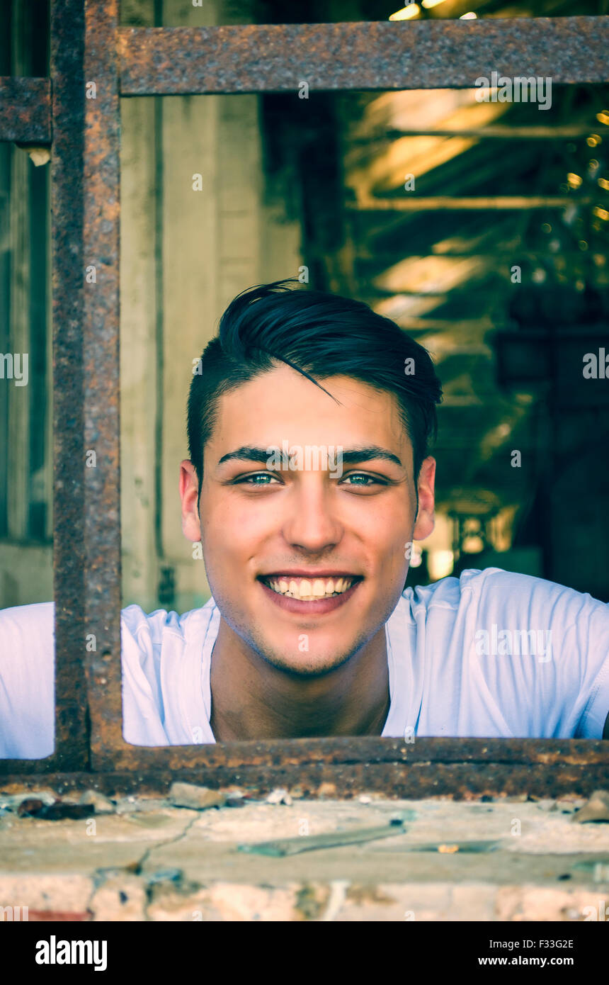 Attractive young man at rusty window with happy expression on his face ...