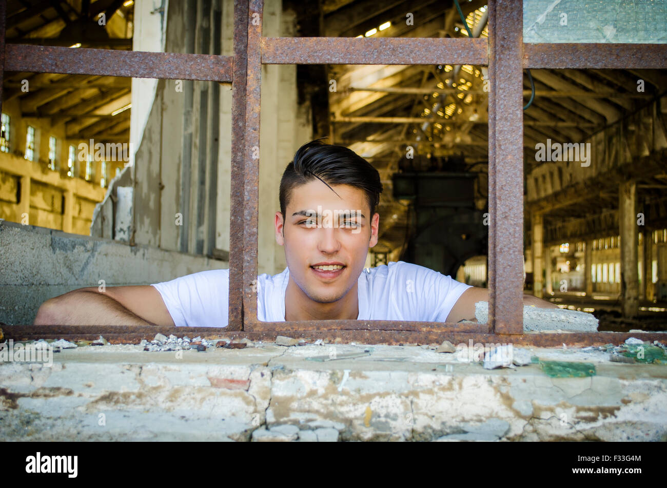 Attractive young man at rusty window with happy expression on his face ...
