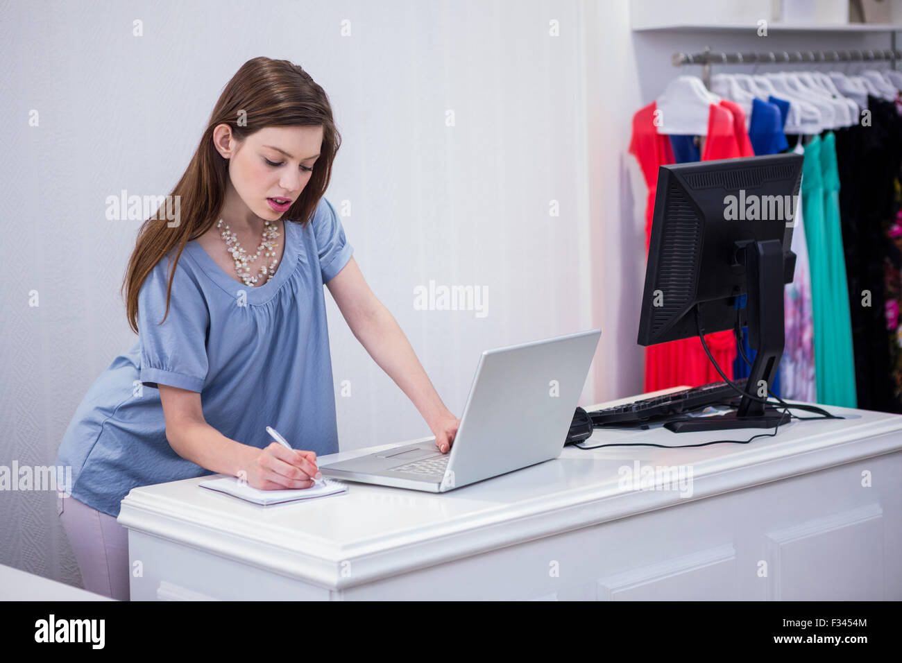 Shop worker using laptop by the till Stock Photo - Alamy