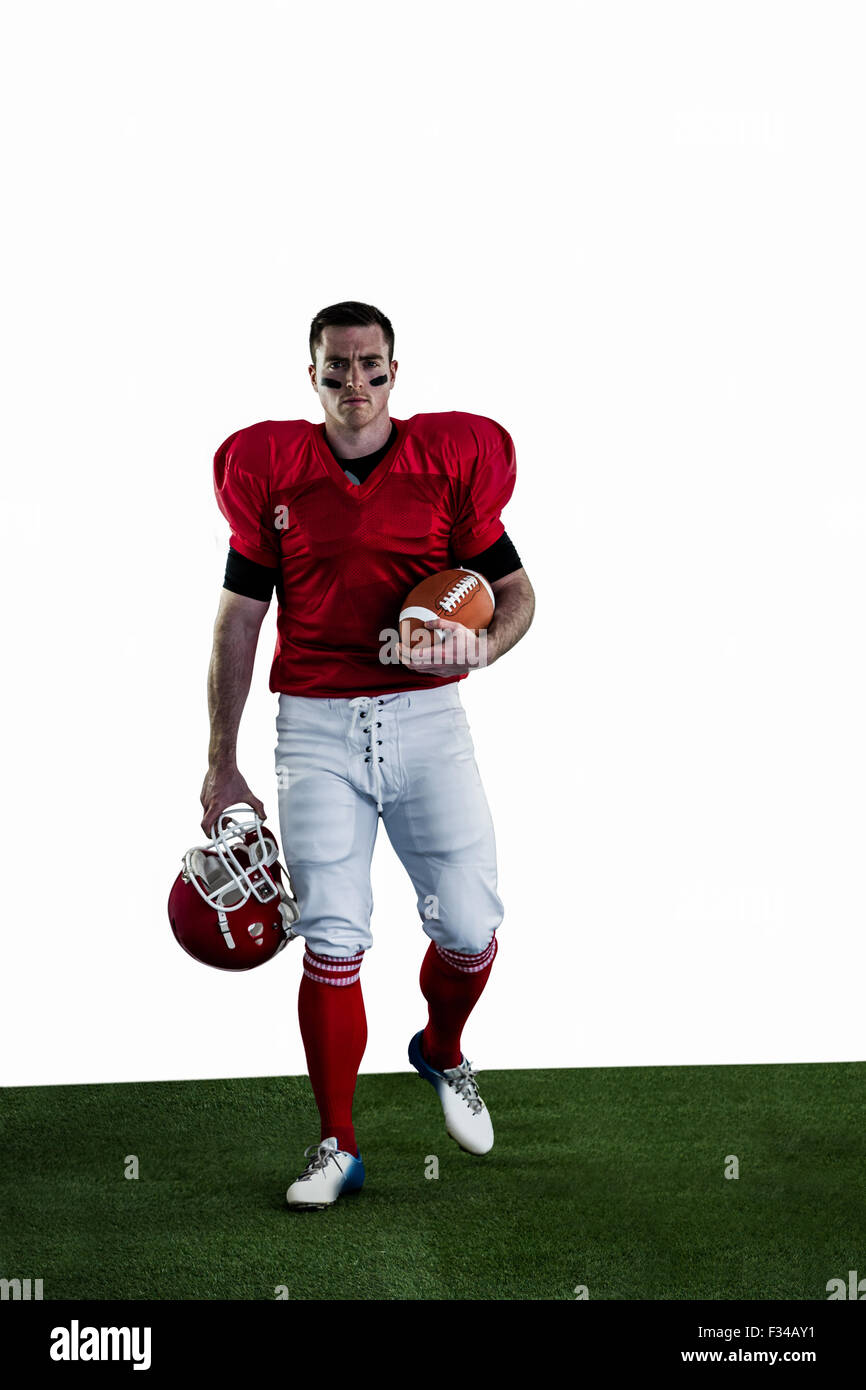 Portrait of american football player walking and holding football and ...