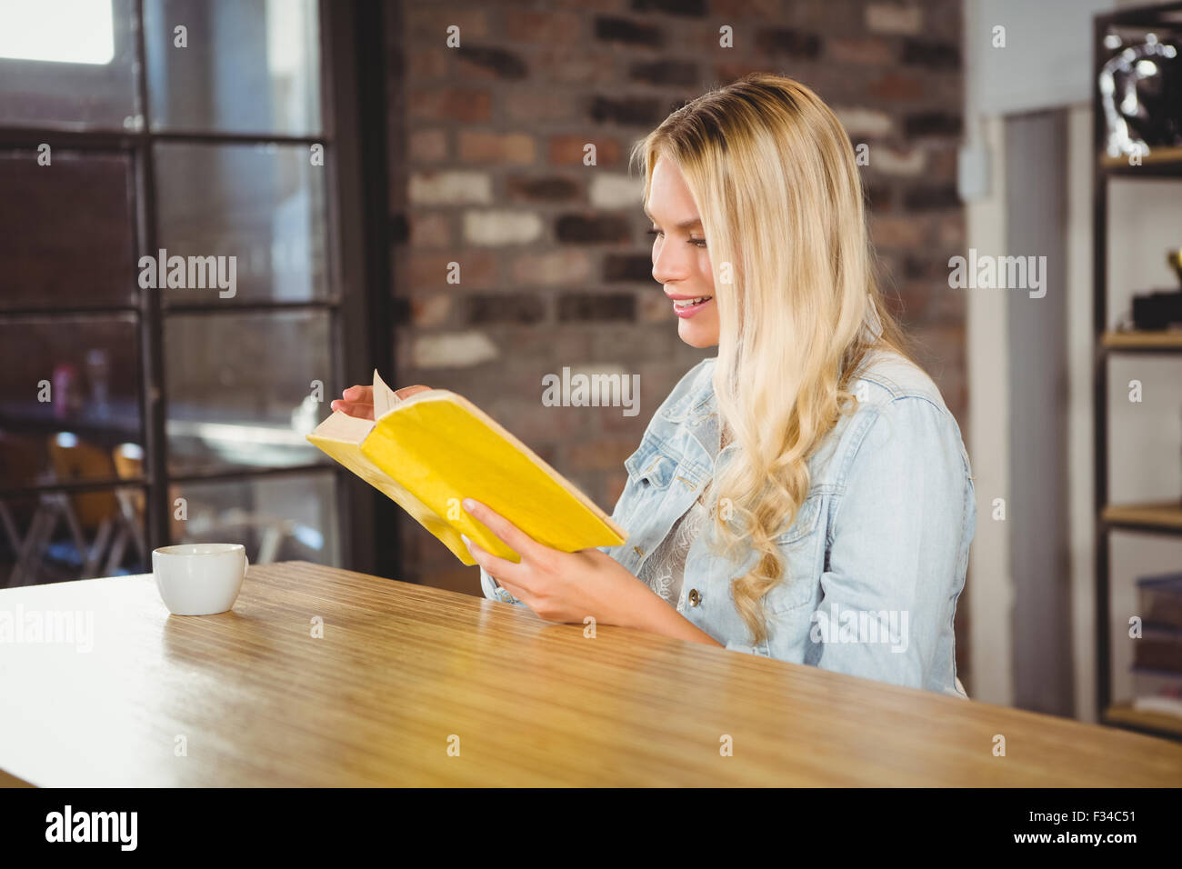 Smiling blonde reading yellow book Stock Photo - Alamy