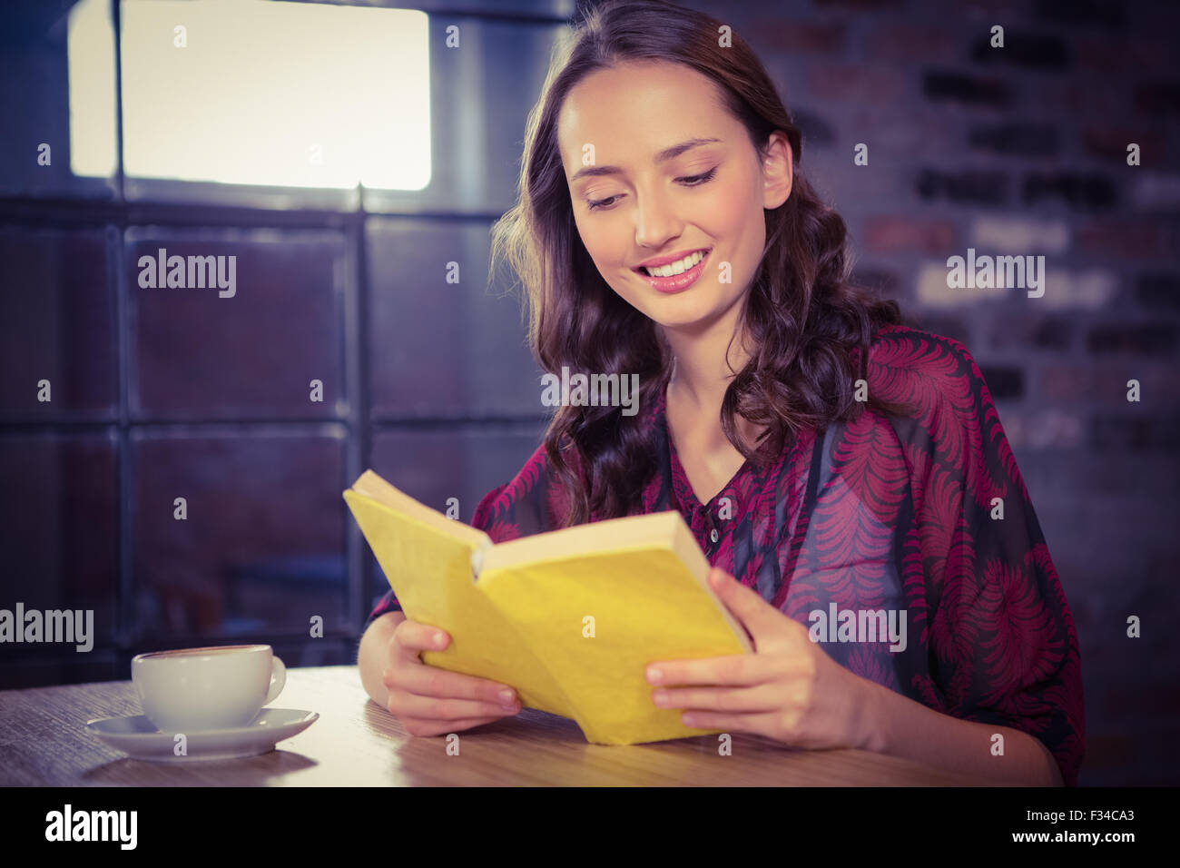 Smiling brunette reading yellow book Stock Photo - Alamy