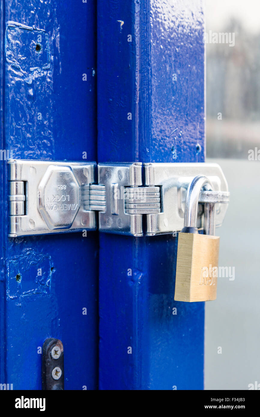 Golden colour padlock on silver lock on blue painted door frame. Close ...