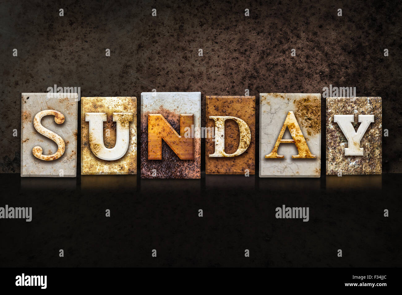 The word "SUNDAY" written in rusty metal letterpress type on a dark ...