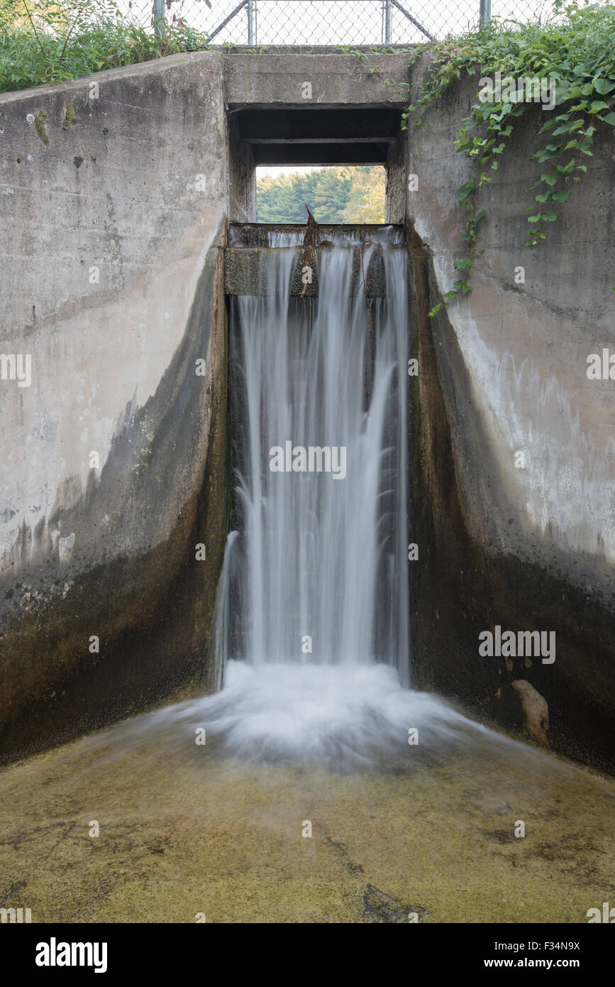 Waters streams over the spillway of a small concrete dam that blocks ...