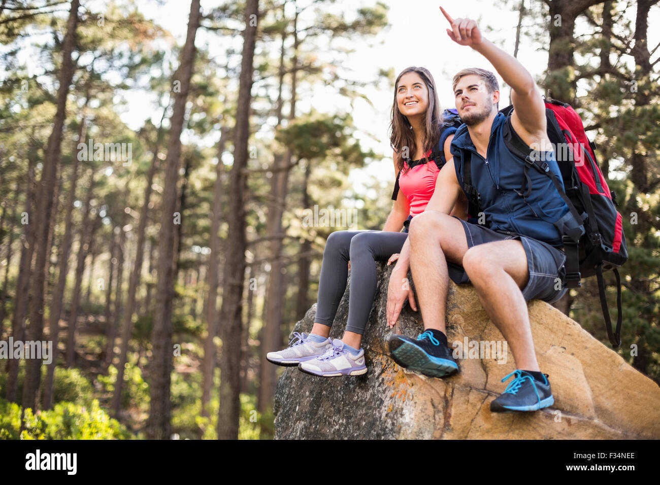 Young happy joggers sitting on rock feeling and pointing at something ...