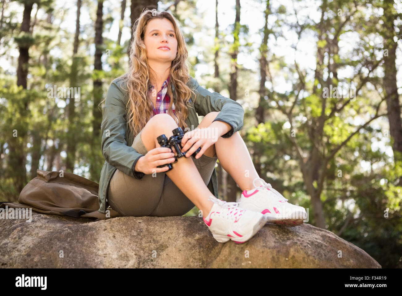 Pretty blonde hiker with binoculars sitting on stone Stock Photo - Alamy