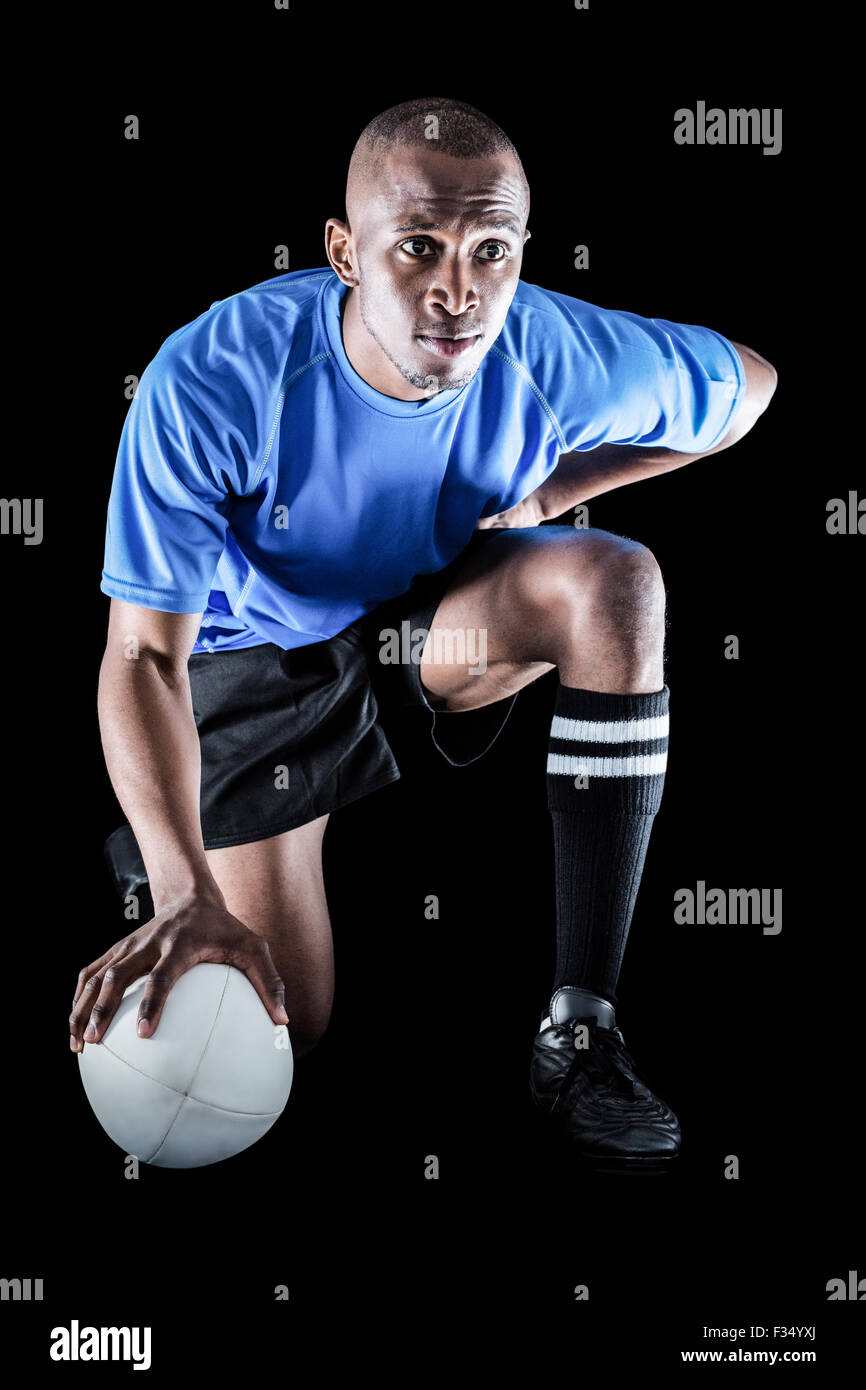 Serious rugby player kneeling while holding ball Stock Photo - Alamy