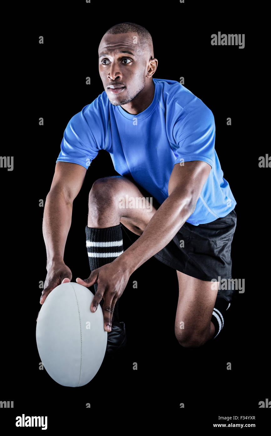 Rugby player holding ball while kneeling Stock Photo - Alamy