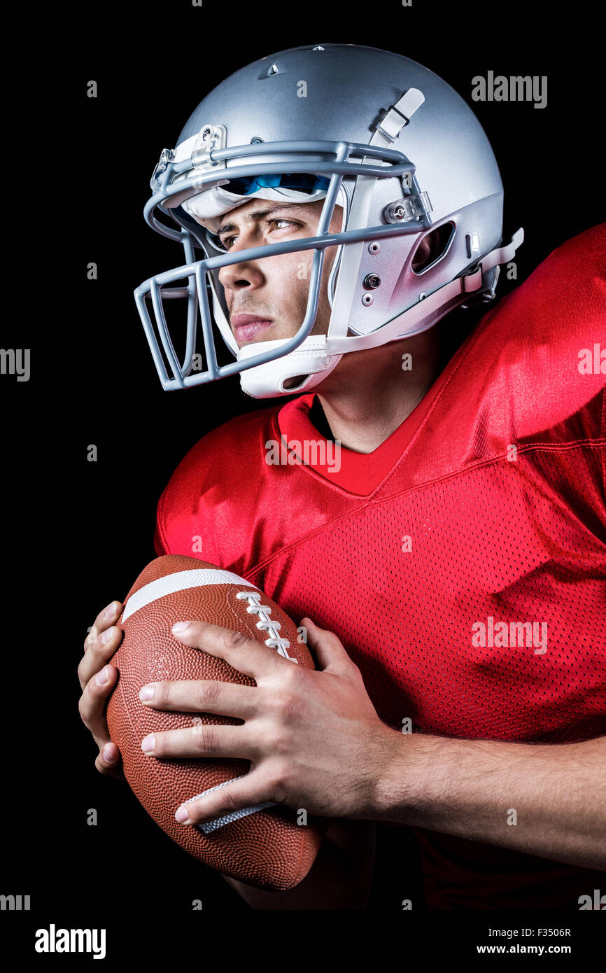 Determined American football player looking away while holding ball ...
