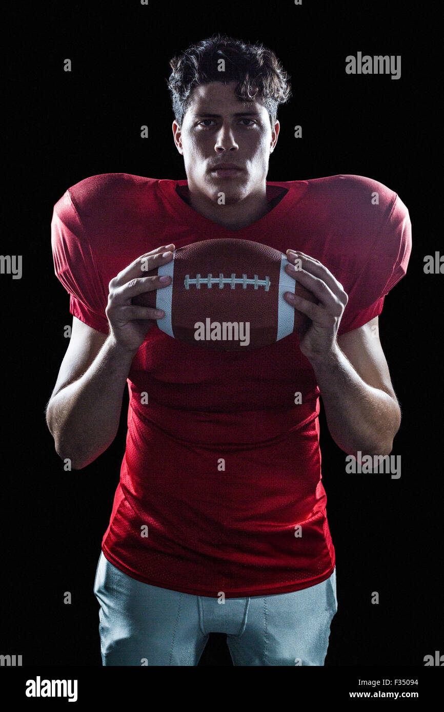 Portrait of determined American football player with ball standing ...
