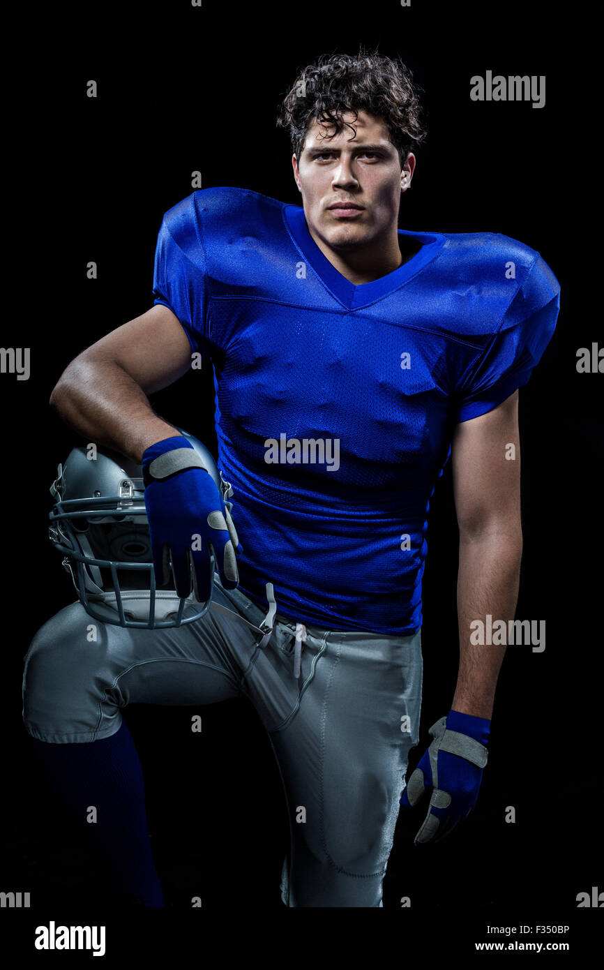 Portrait of determined American football player with hand on helmet ...