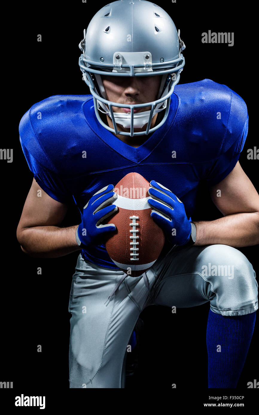 Determined American football player holding ball while kneeling Stock ...
