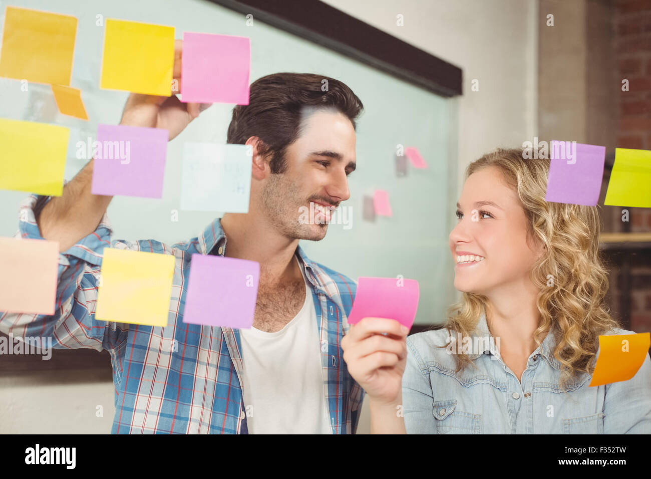 Smiling business people touching sticky notes on glass in office Stock ...