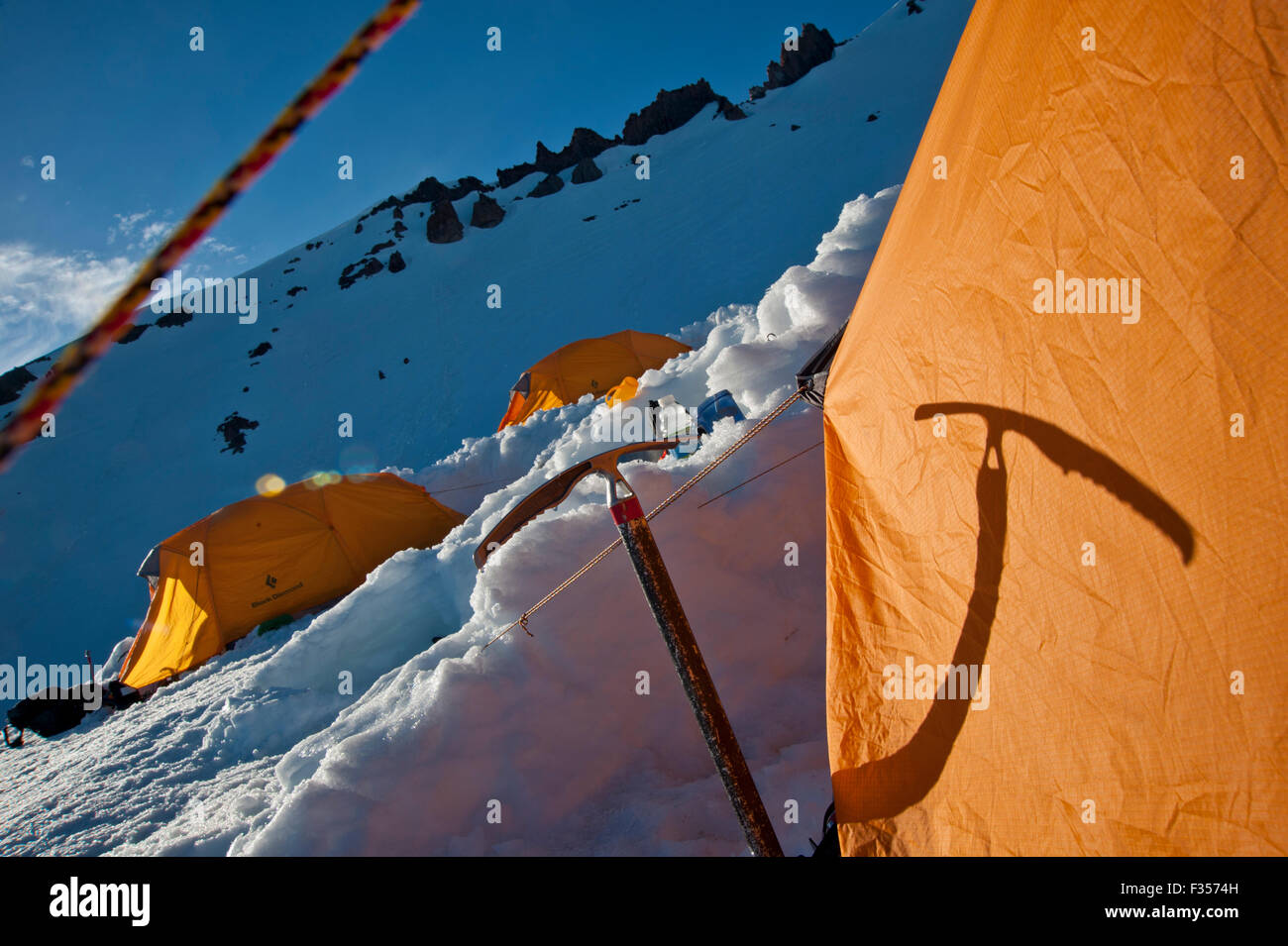 Evening sun casts the shadow of an ice ax on a tent on Mount Shasta ...