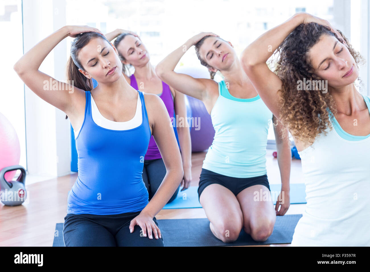 Women doing head exercise while kneeling in fitness studio Stock Photo ...