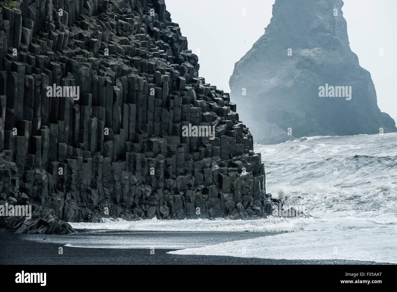 Wave about to hit stacked basalt rocks on the black lava beach in Vik ...