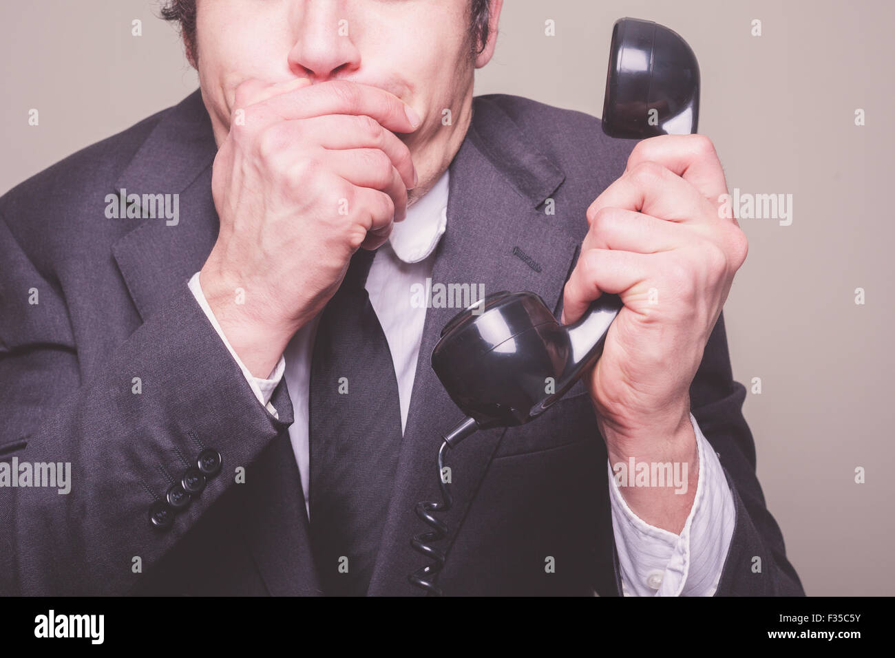 A young businessman is on the phone and covering his mouth in shock ...