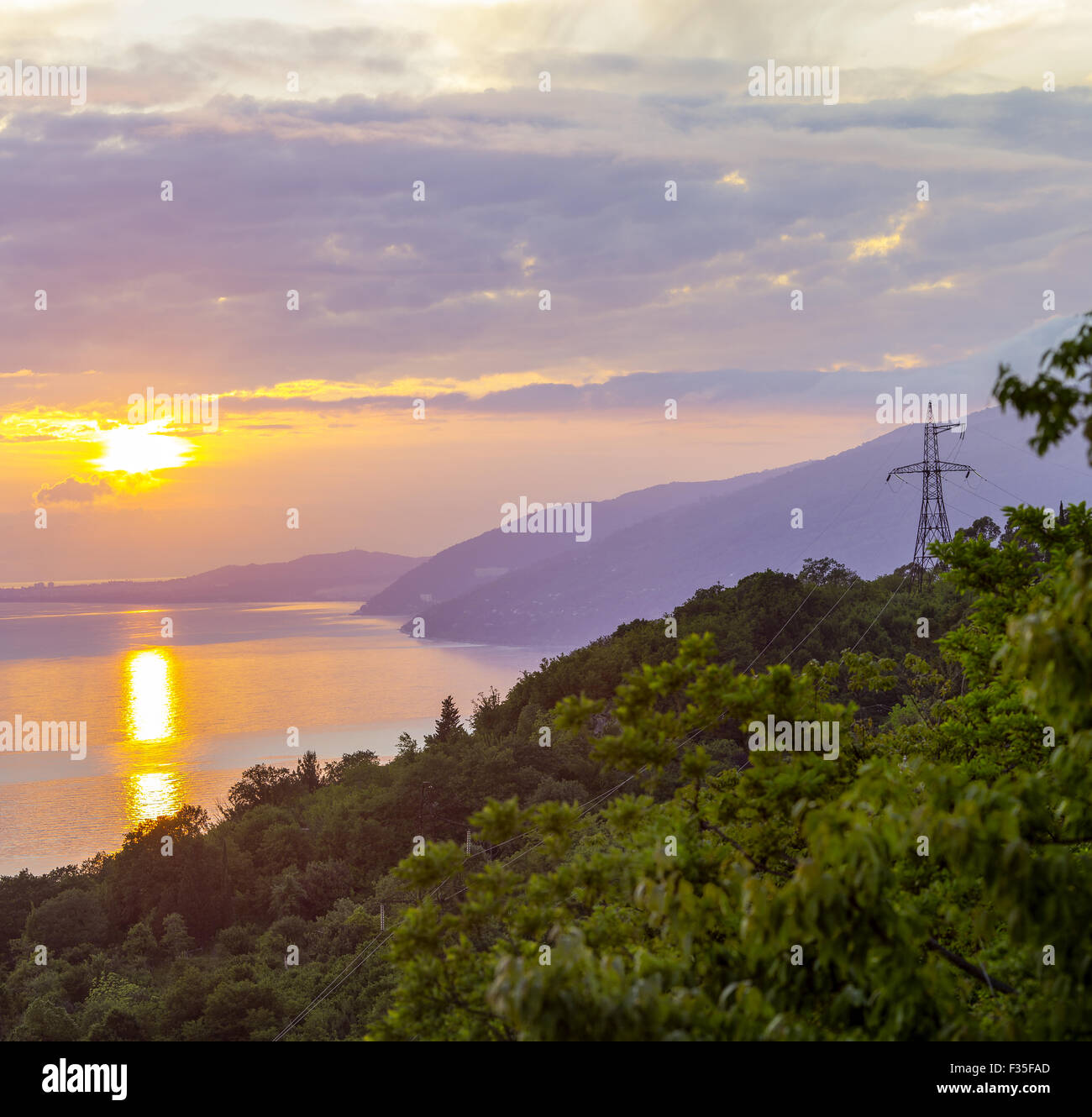 Overhead power transmission line in mountains with sea and sunset on ...