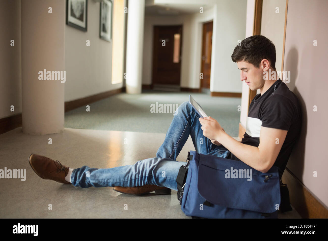 Male student using digital tablet sitting by wall Stock Photo - Alamy