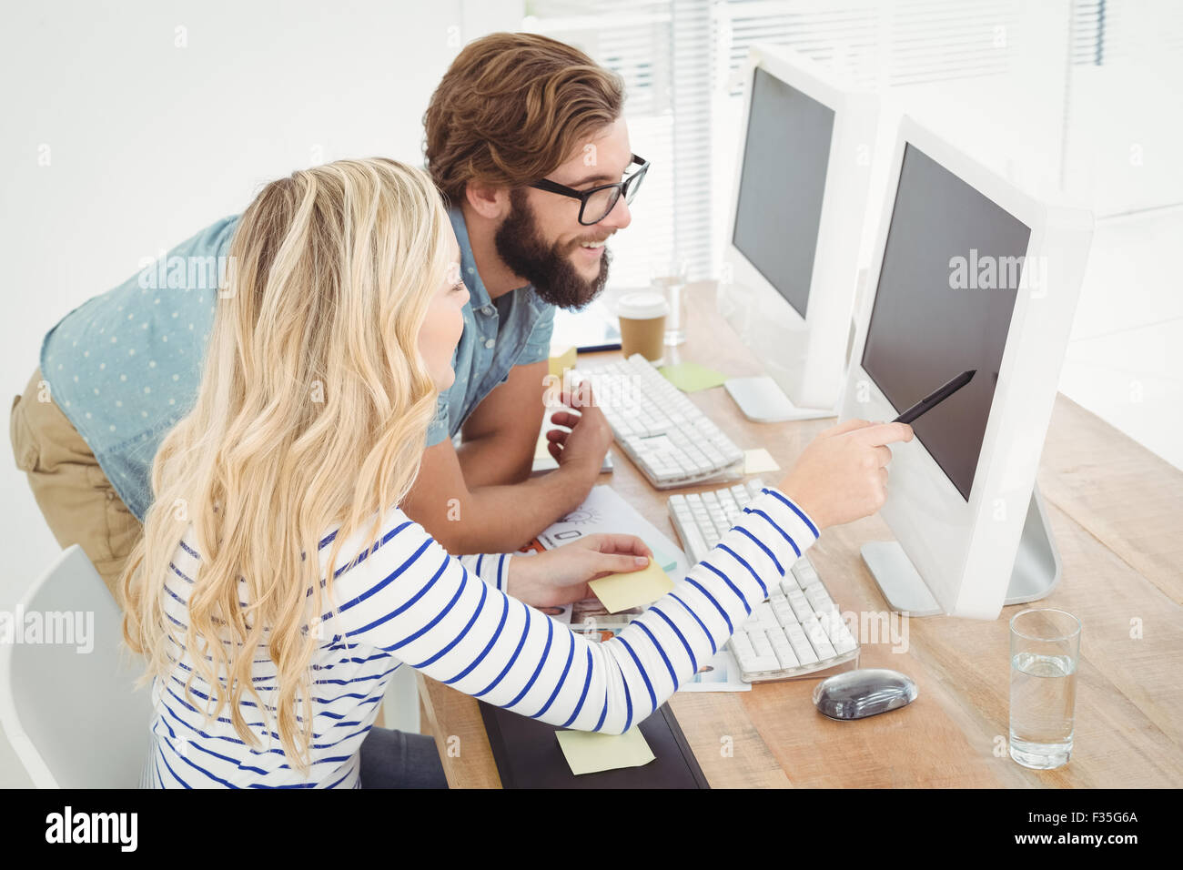 Woman pointing at computer with stylus while sitting by man Stock Photo ...