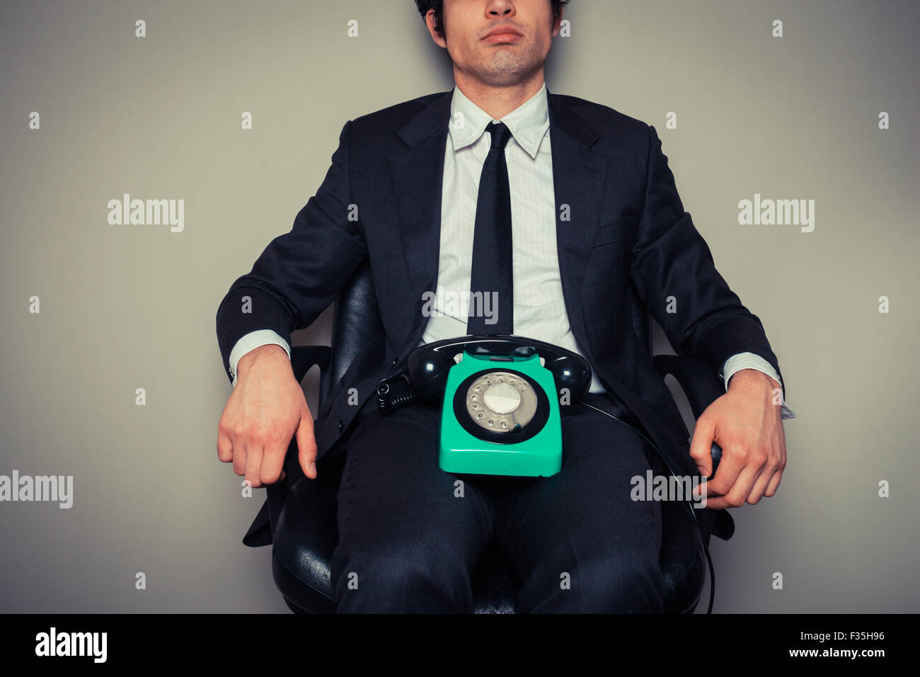 A young businessman is sitting in an office chair with an old rotary ...