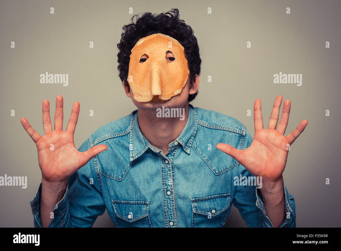 Young man has cut eyeholes in a pancake and is wearing it on his face ...