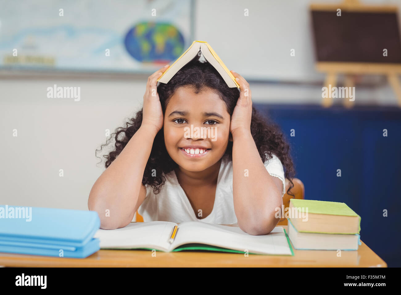 Smiling pupil holding book on head in a classroom Stock Photo - Alamy