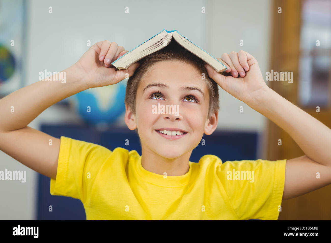Smiling pupil holding book on head in a classroom Stock Photo - Alamy