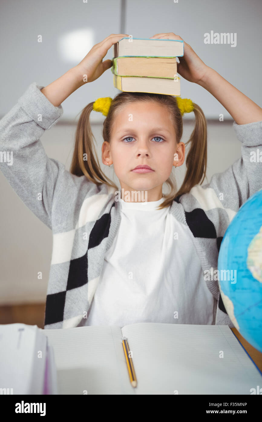 Cute pupil balancing books on head in a classroom Stock Photo - Alamy
