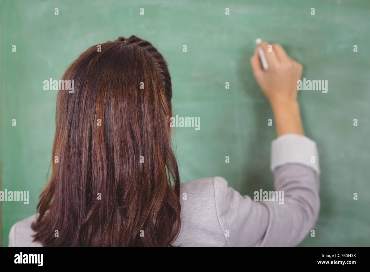 Rear view of teacher writing on chalkboard in a classroom Stock Photo ...
