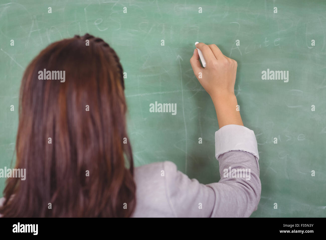 Rear view of teacher writing on chalkboard in a classroom Stock Photo ...