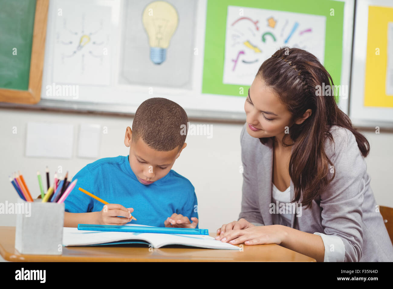 Pretty teacher helping pupil at his desk Stock Photo - Alamy