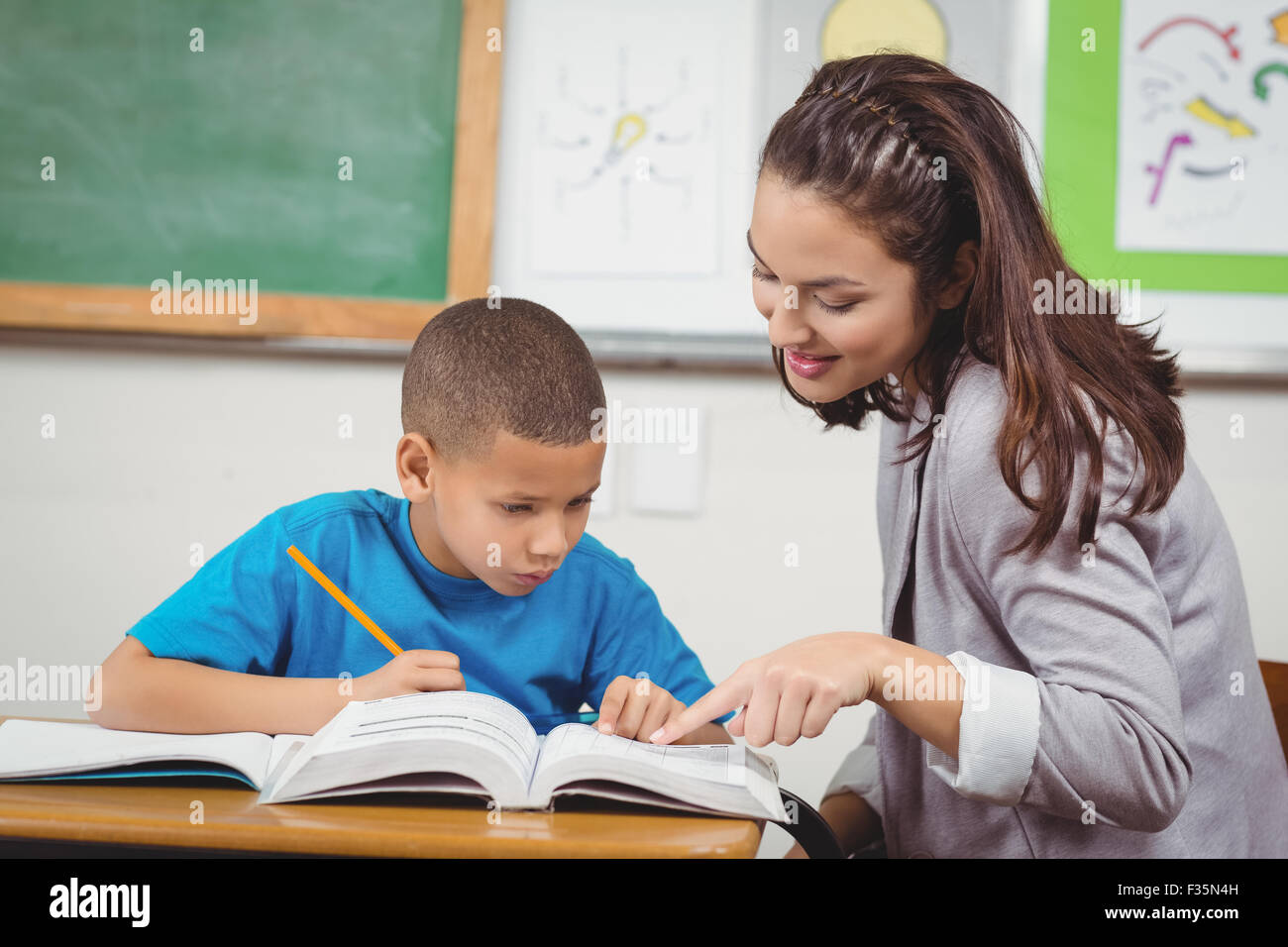 Pretty teacher helping pupil at his desk Stock Photo - Alamy