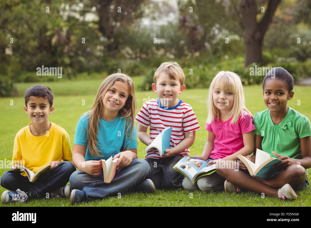 Smiling classmates sitting in grass and holding books Stock Photo - Alamy