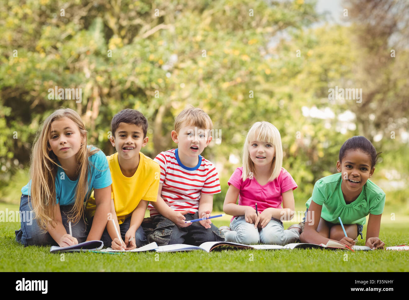 Smiling classmates sitting in grass and studying Stock Photo - Alamy