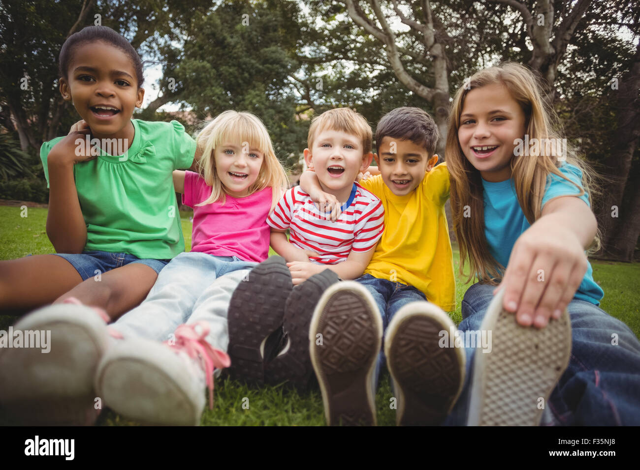 Happy classmates sitting in grass and having arms around Stock Photo ...