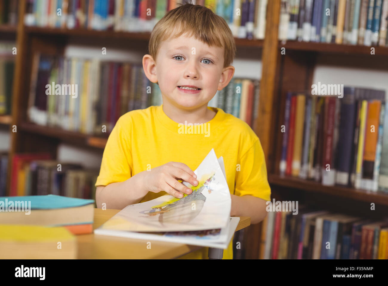 Smiling pupil reading book in the library Stock Photo - Alamy